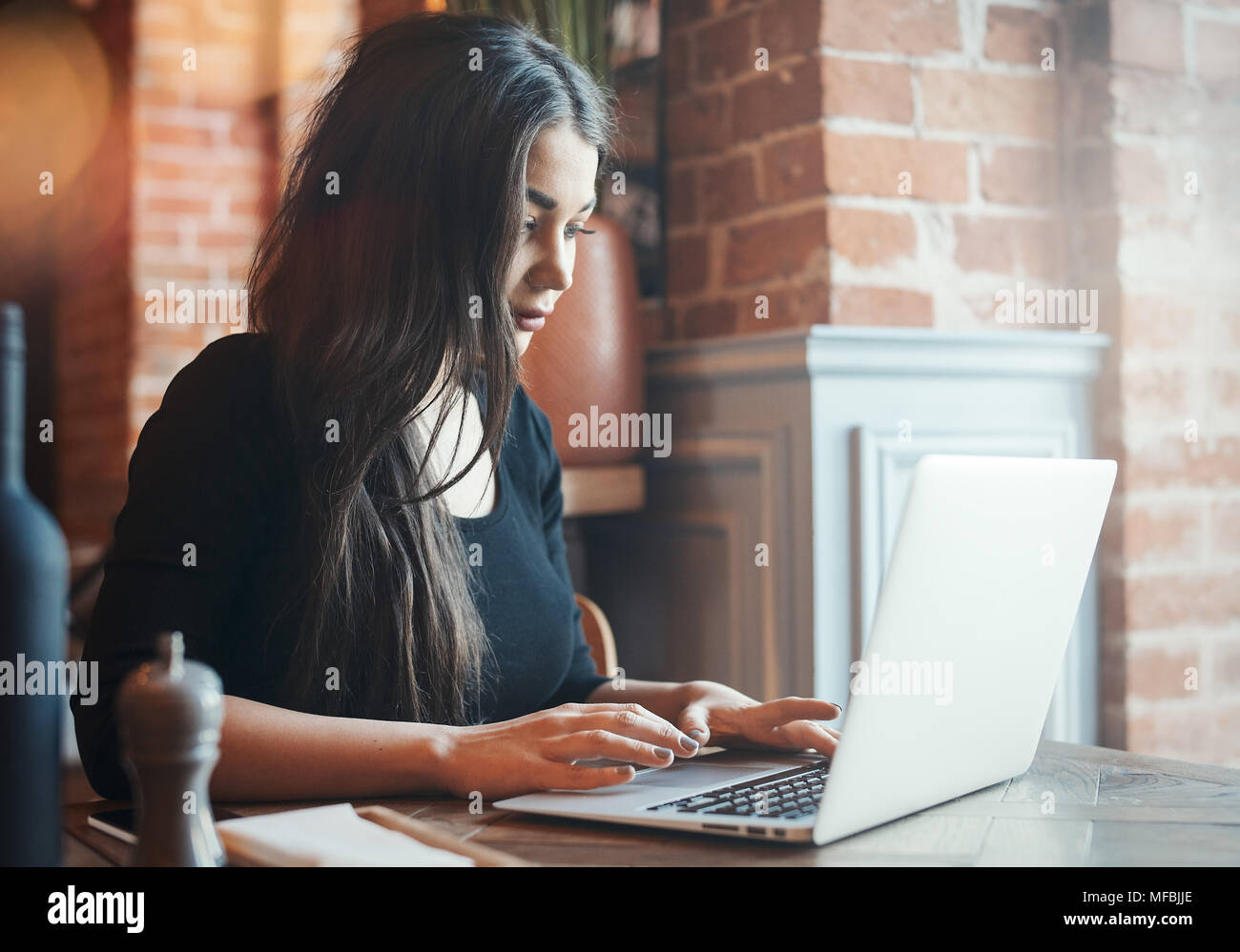 Pensive young woman working on laptop in cafe. Girl is on focus and ...