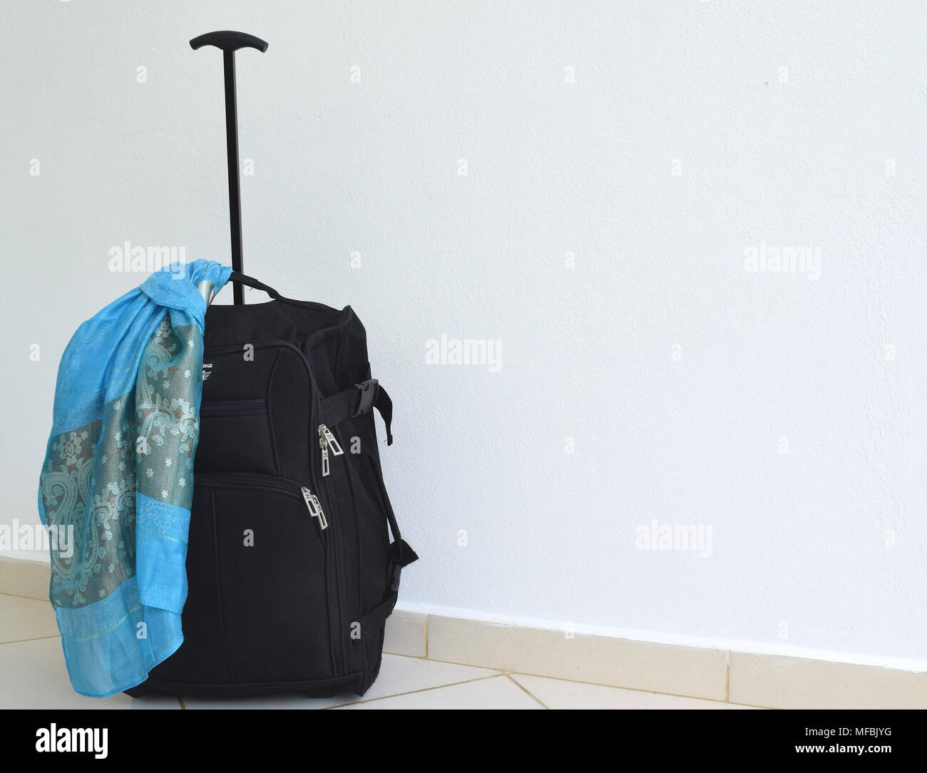 Black suitcase with a beautiful silk scarf on white textured background ...