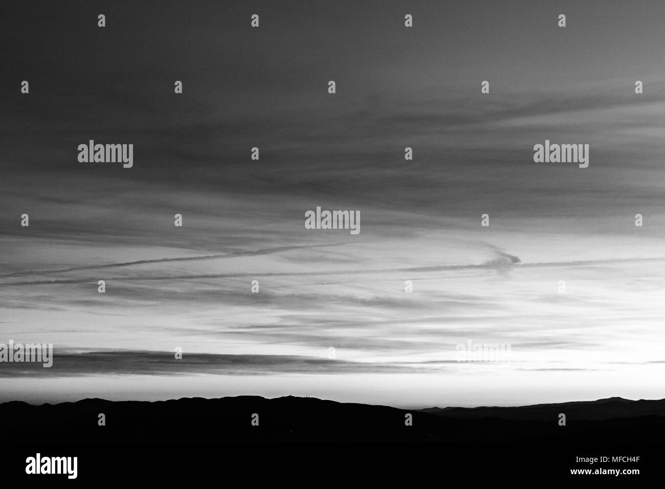 Sunset over distant mountains, with deep sky full of white clouds and ...