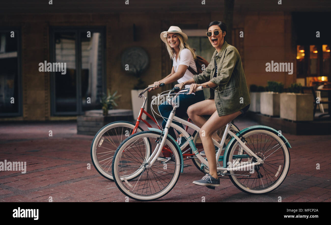 Female friends riding their bicycles on city street. Two women enjoying ...