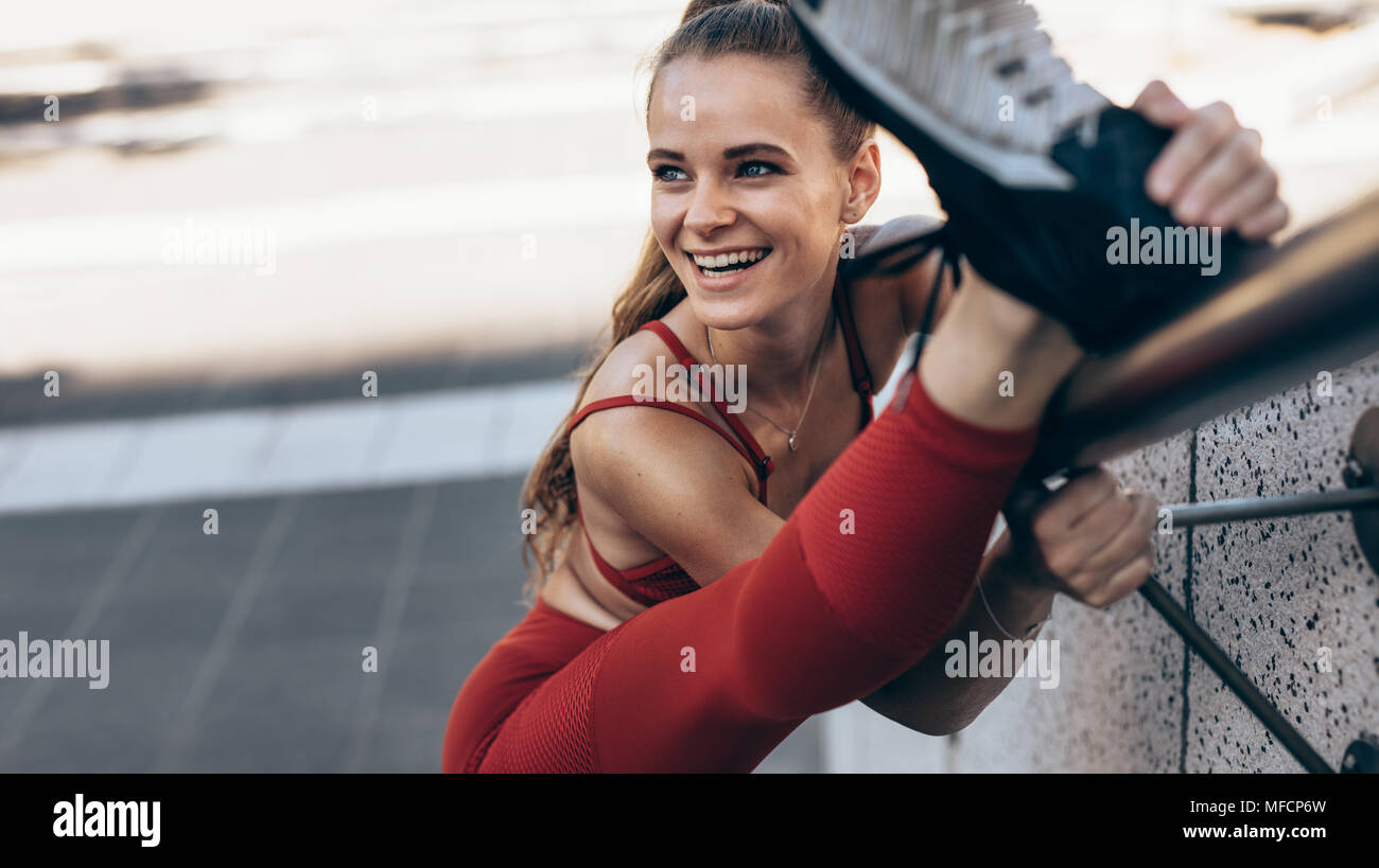 Fit sportswoman doing leg stretches on a railing. Female athlete doing ...