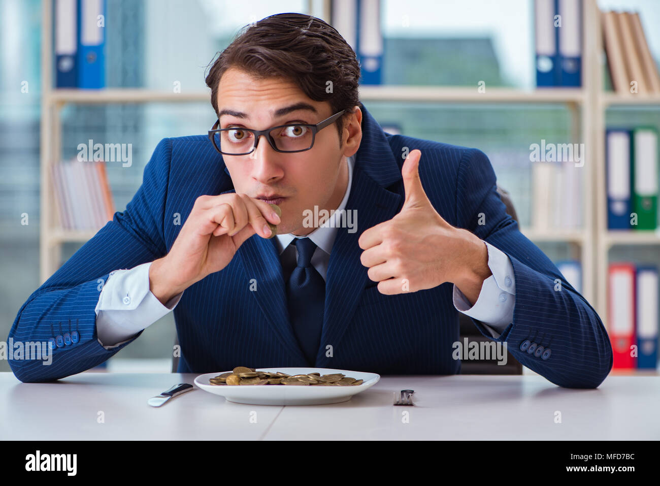Funny businessman eating gold coins in office Stock Photo - Alamy