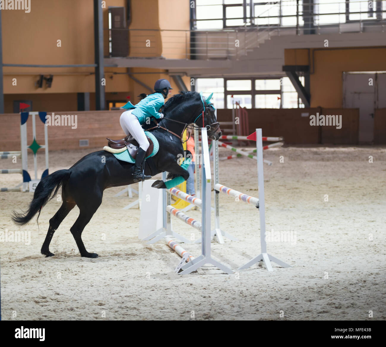 Young woman on the black stallion jumping over hurdle at show jumping ...