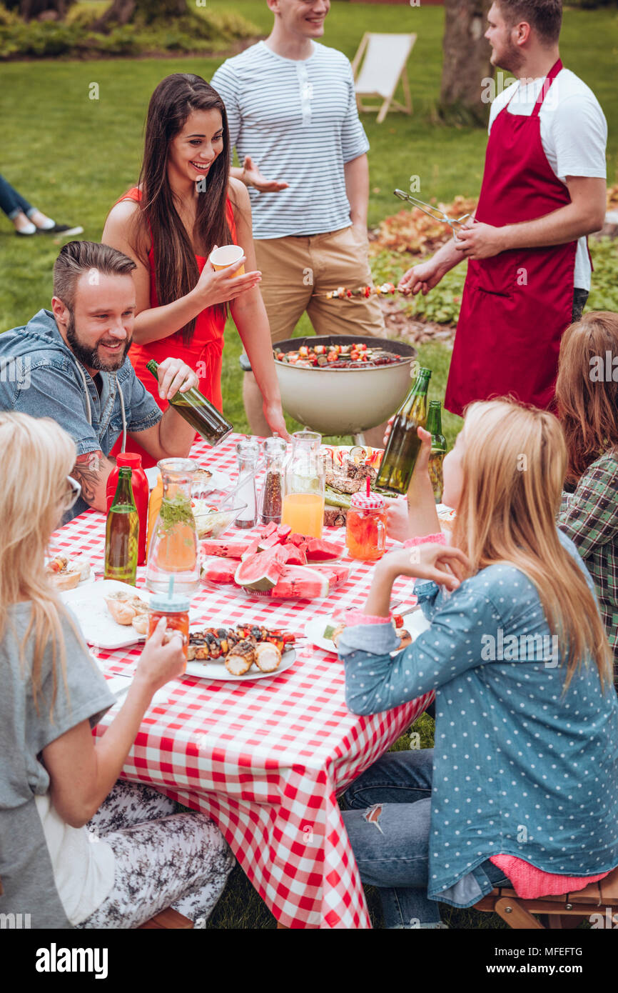 Group of friends in the backyard enjoying a meal, eating and drinking ...