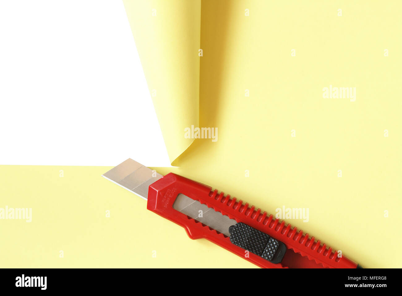 Red office knife cutting yellow paper sheet. Isolated on white with ...