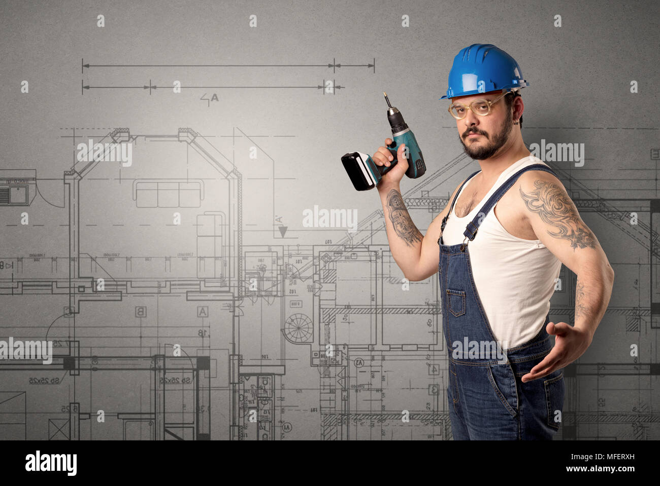 Worker standing with tool in his hand in front of technical drawings ...