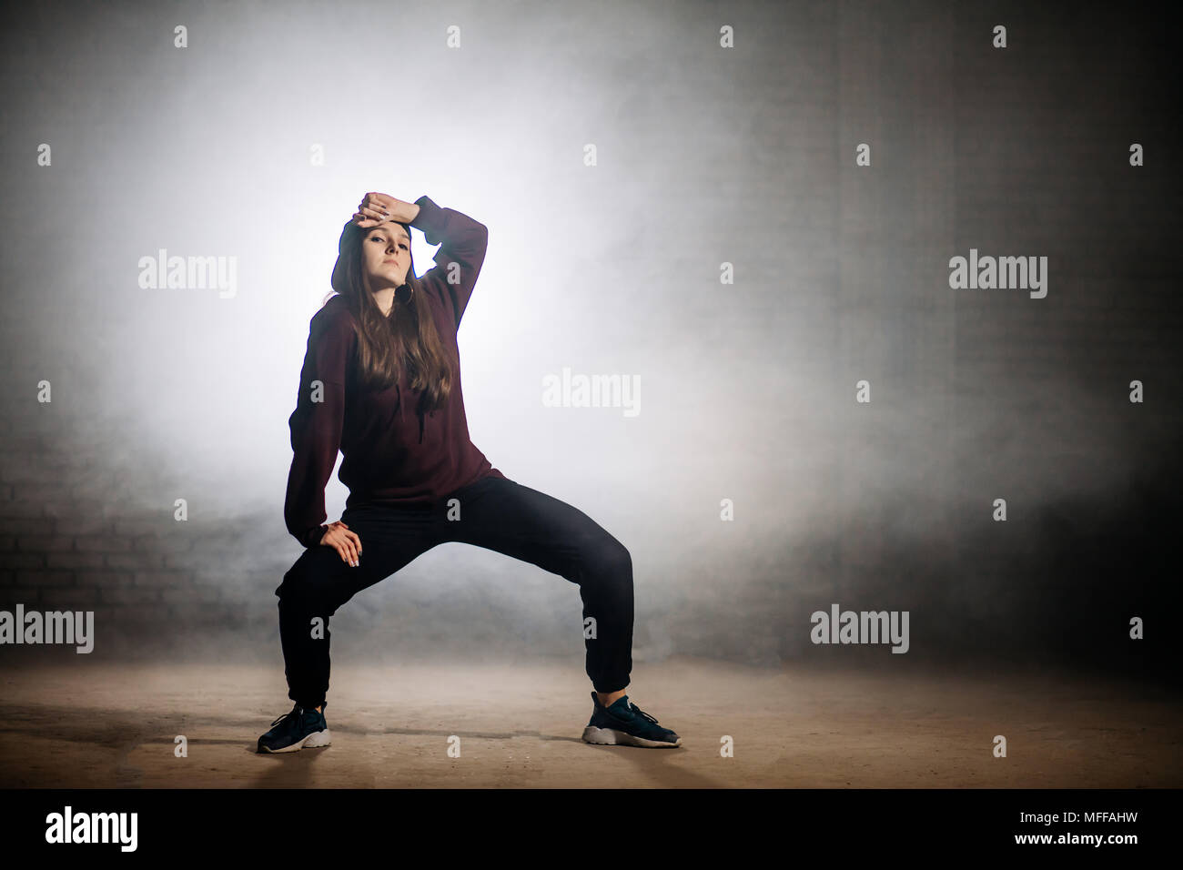 Caucasian girl with spread legs dancing hip hop on the dark background ...