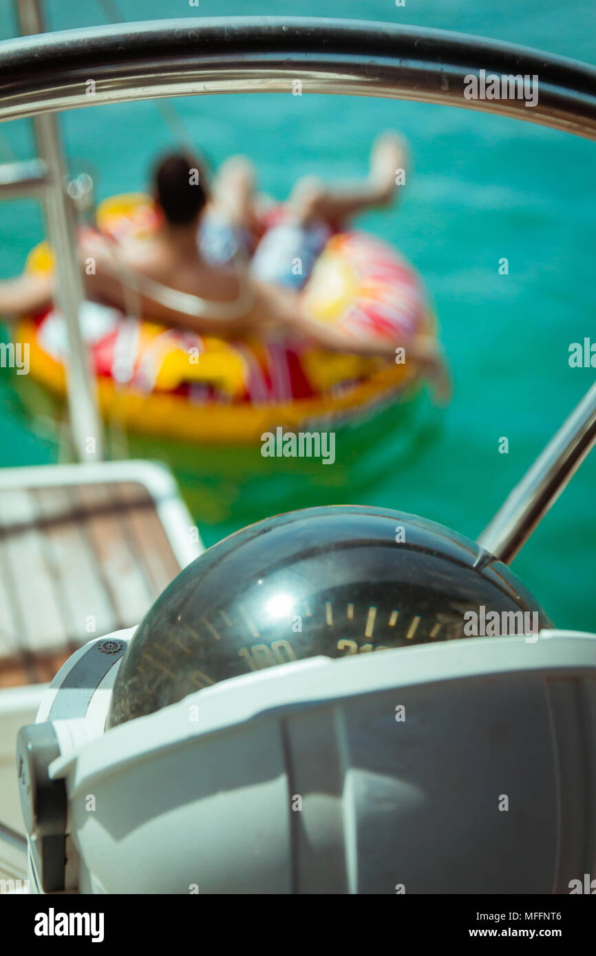 Compass on a yacht boat. In the background there is a man floating in ...