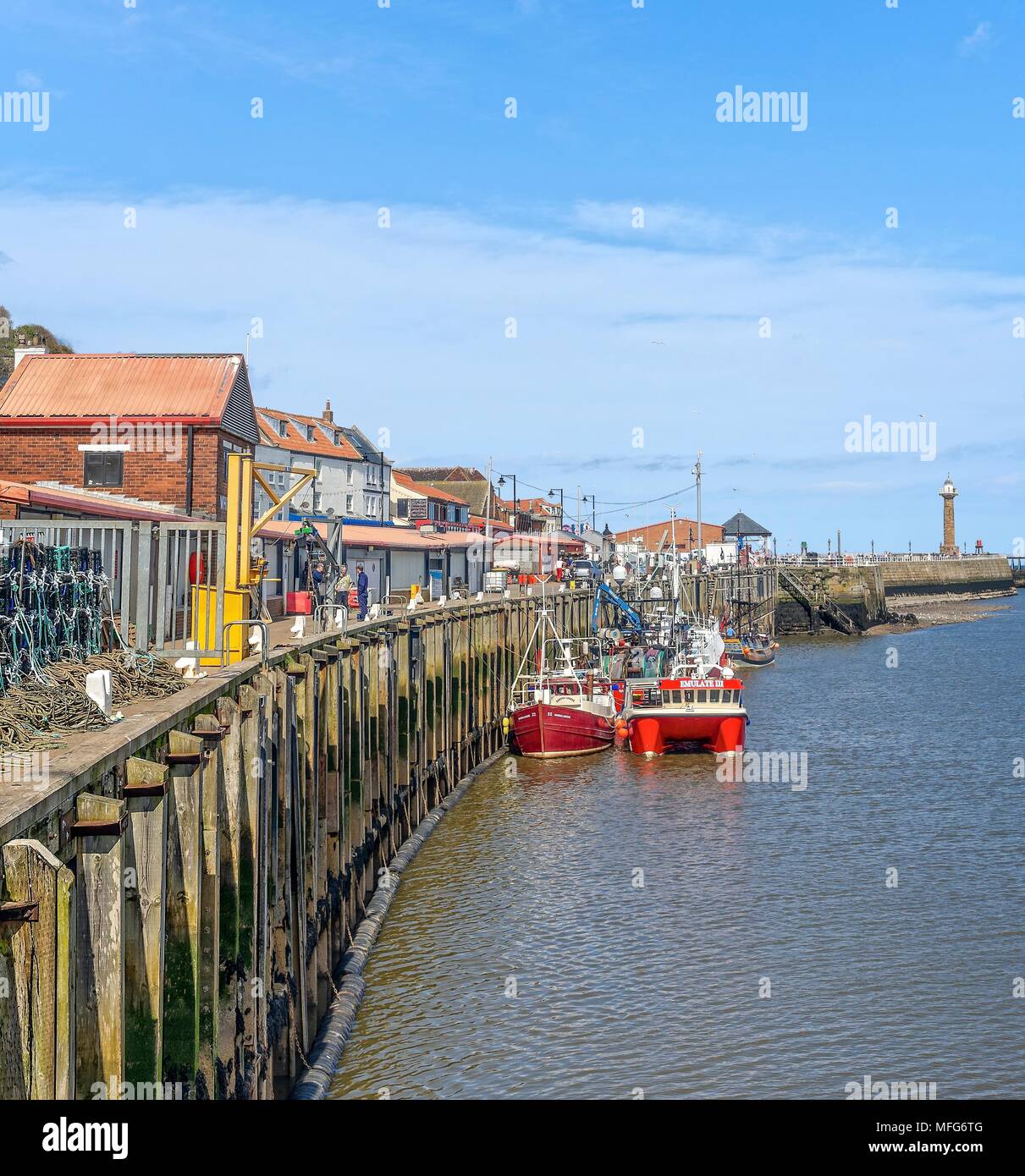 Two fishing boats moored alongise the quay in Whitby. A lighthouse is ...