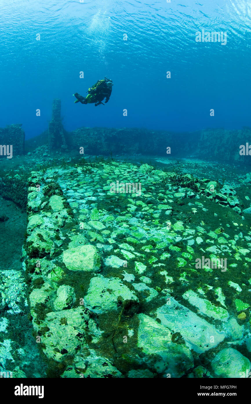 Scuba diver swimming over a old road, between walls of the underwater ...