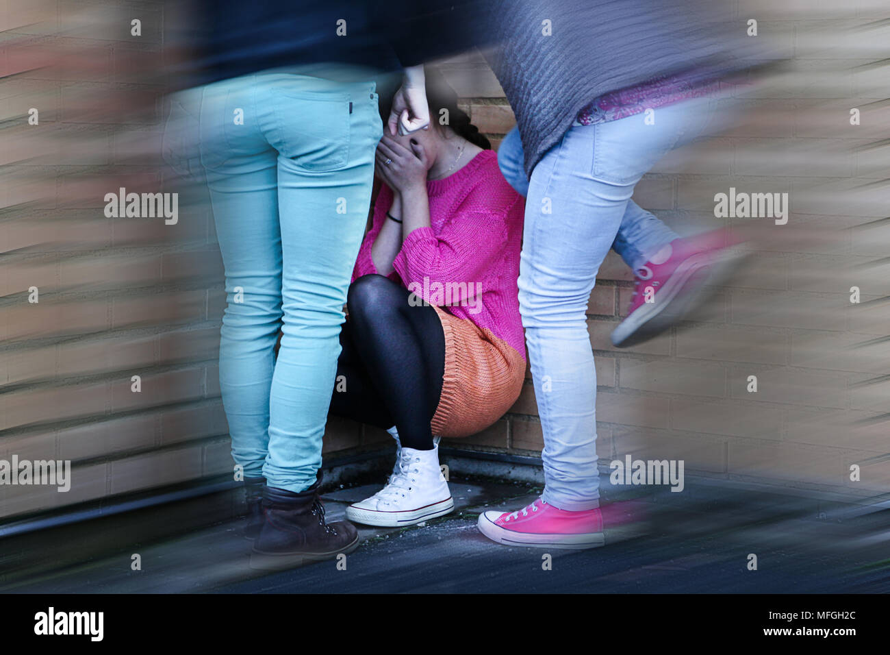 Teenage Girls Bullying And Kicking A Girl Sitting Down Covering Her