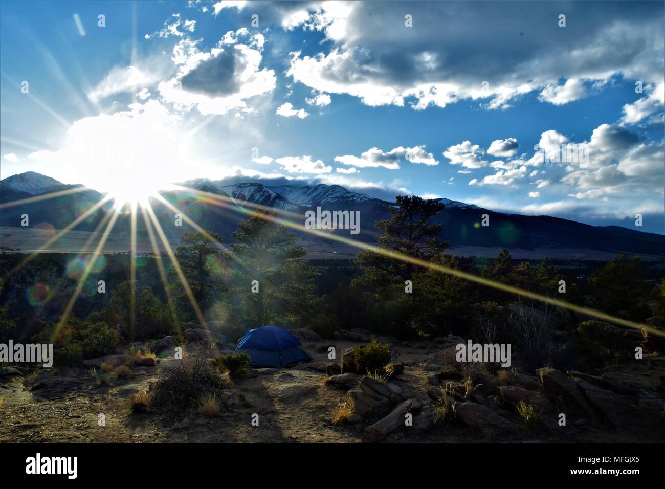 Sun rays over campsite with tent and mountains in the distance. Taken ...
