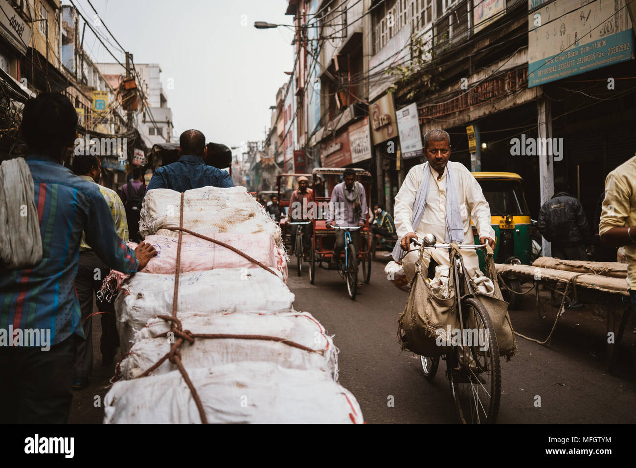 Indian man on his bicycle passing men pushing a cart on a busy street ...