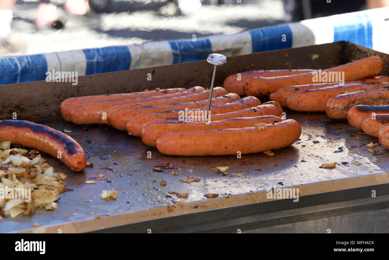 Large hot dogs on an outdoor grill cooking, food thermometer in one ...
