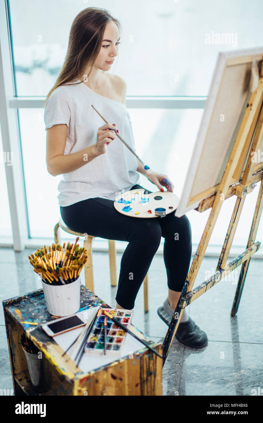 Creative young painter female drawing in art studio using easel ...