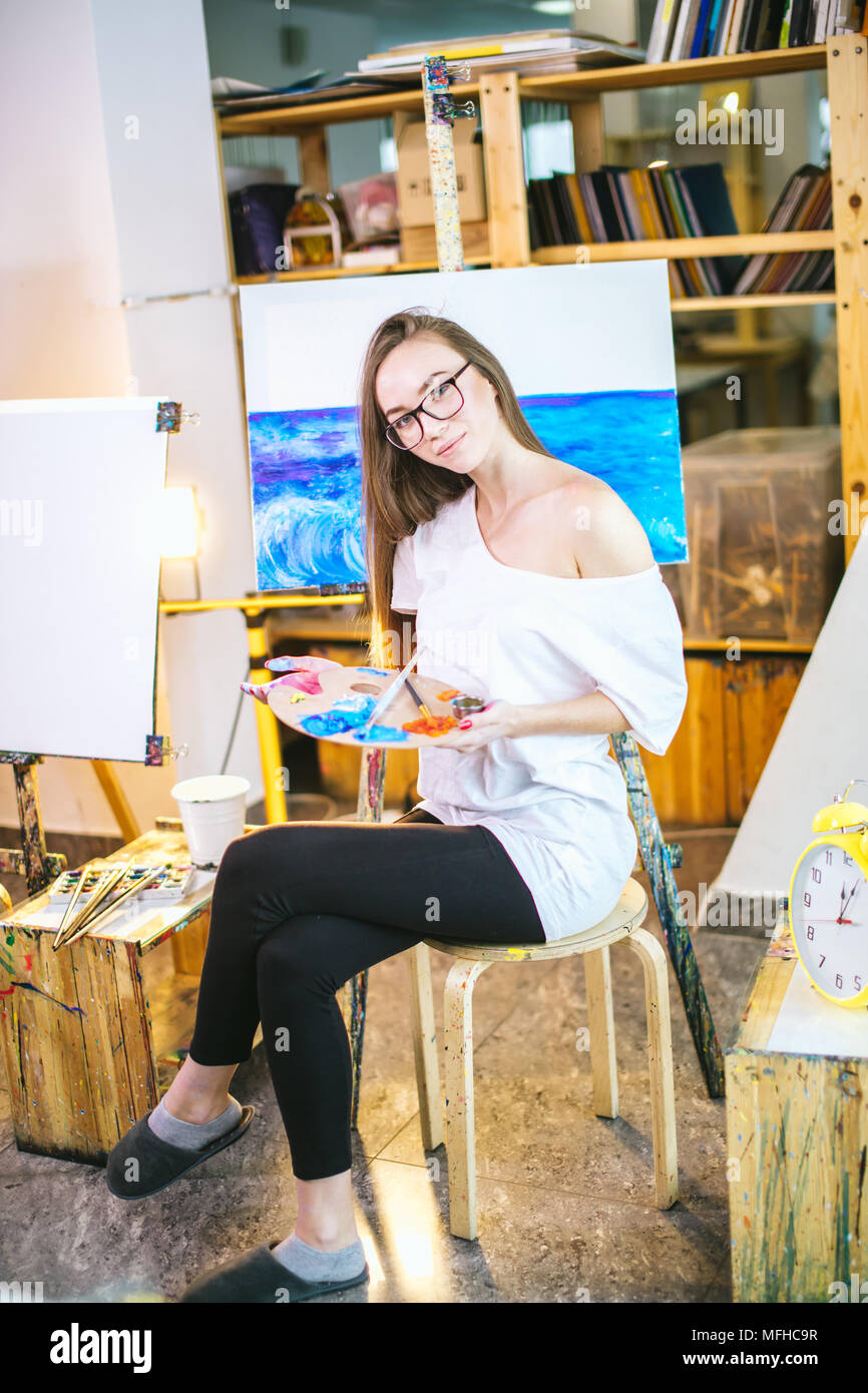 Painting process at studio . Pretty female artist looking at camera ...