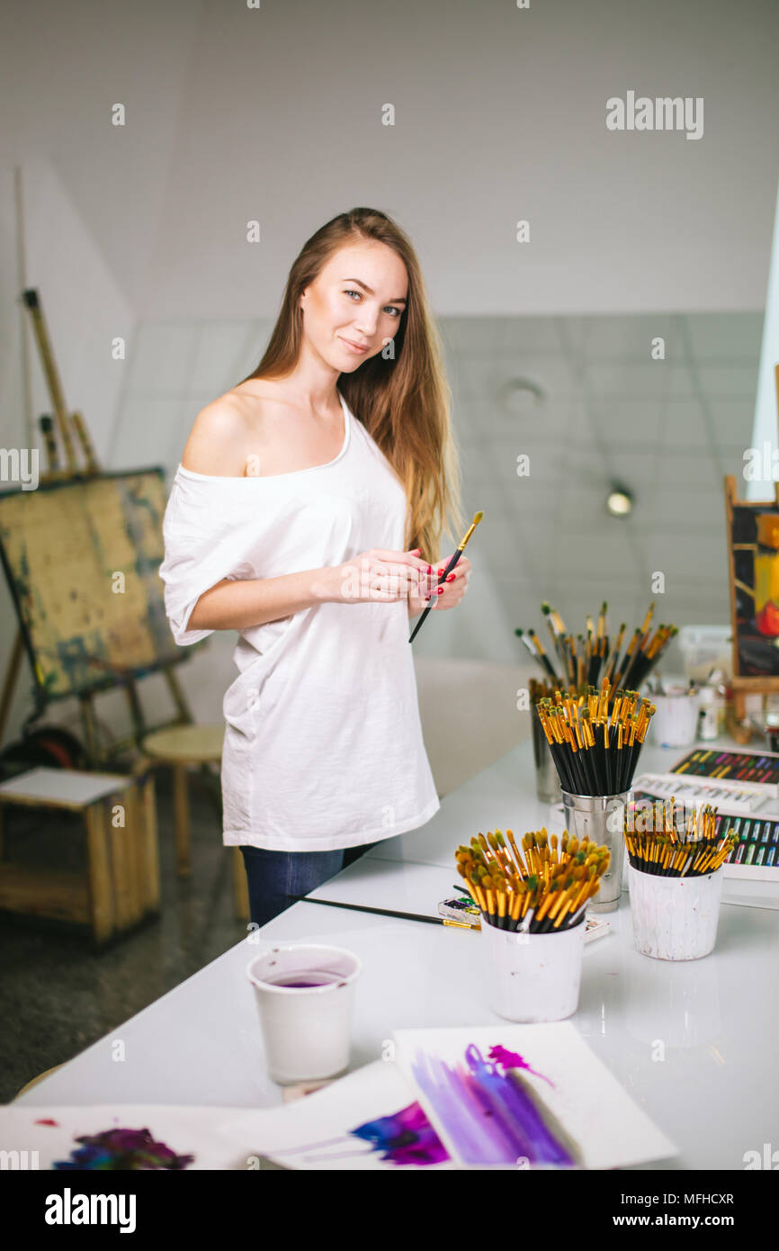 Woman painter in her studio with paintbrush in her hand, looking at ...