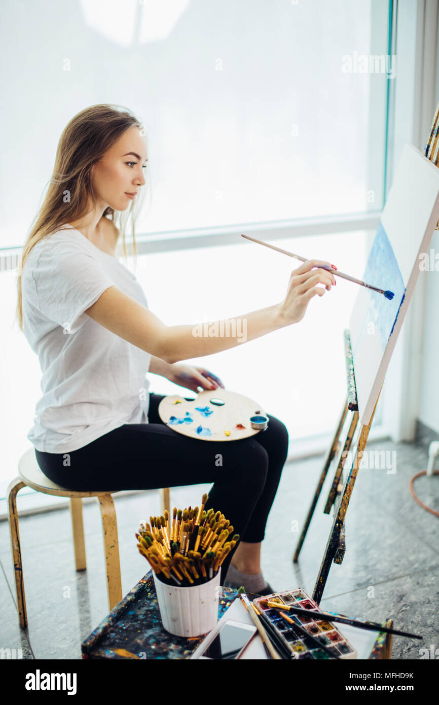 White beautiful female drawing a painting on canvas on easel in art ...