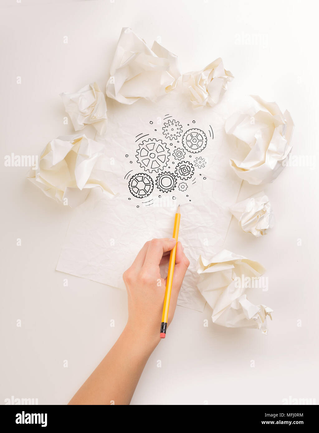 Female hand next to a few crumpled paper balls drawing rotating gears ...
