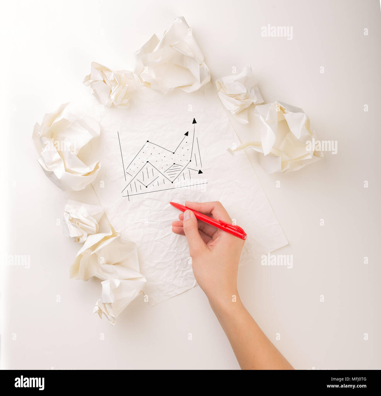 Female hand next to a few crumpled paper balls drawing a progress chart ...
