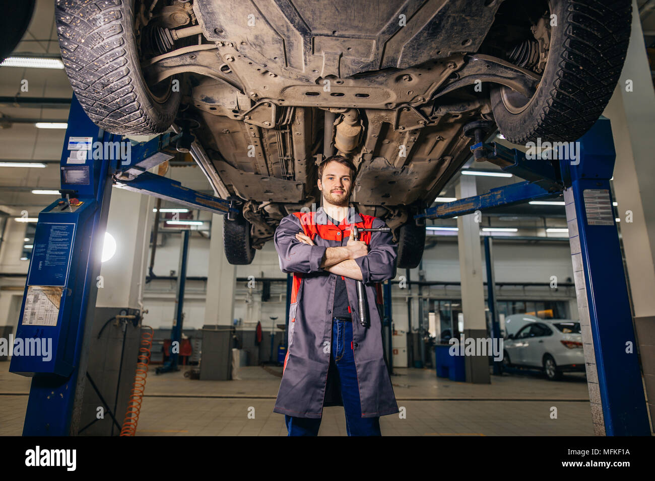 Auto mechanic crossed hands and looking at camera while standing under ...