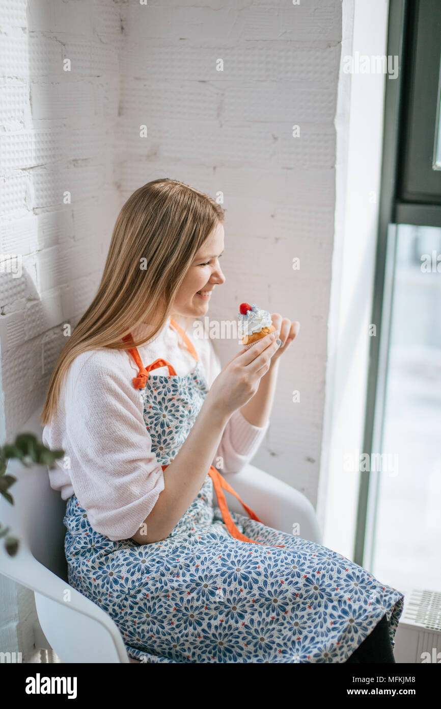 happy Laughing young woman having cupcake while sitting near window ...