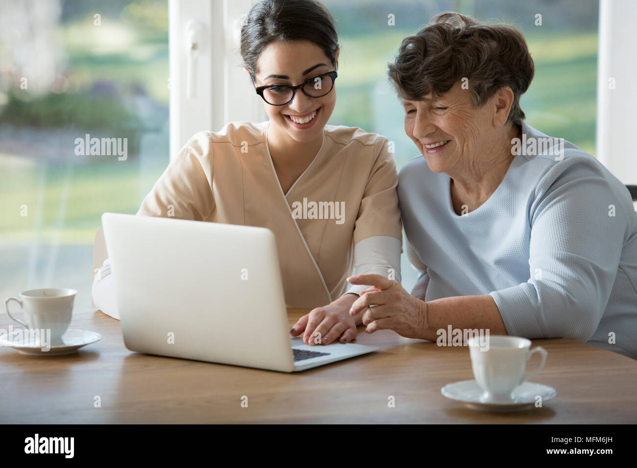 Smiling assistant teaching elderly woman how to use the Internet on a ...
