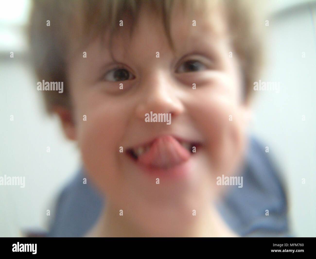 A young boy playing around pulls a funny face for the benefit of the camera. He sticks out his ...