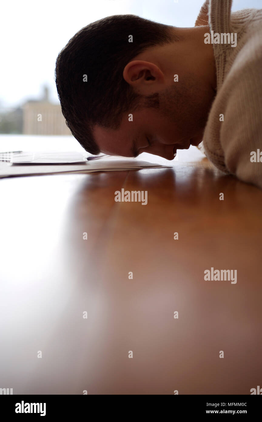 Side profile of a young man bending forward at the table with his eyes ...