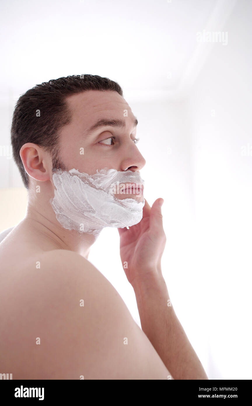 Side profile of a young man applying shaving cream on his face Ref ...