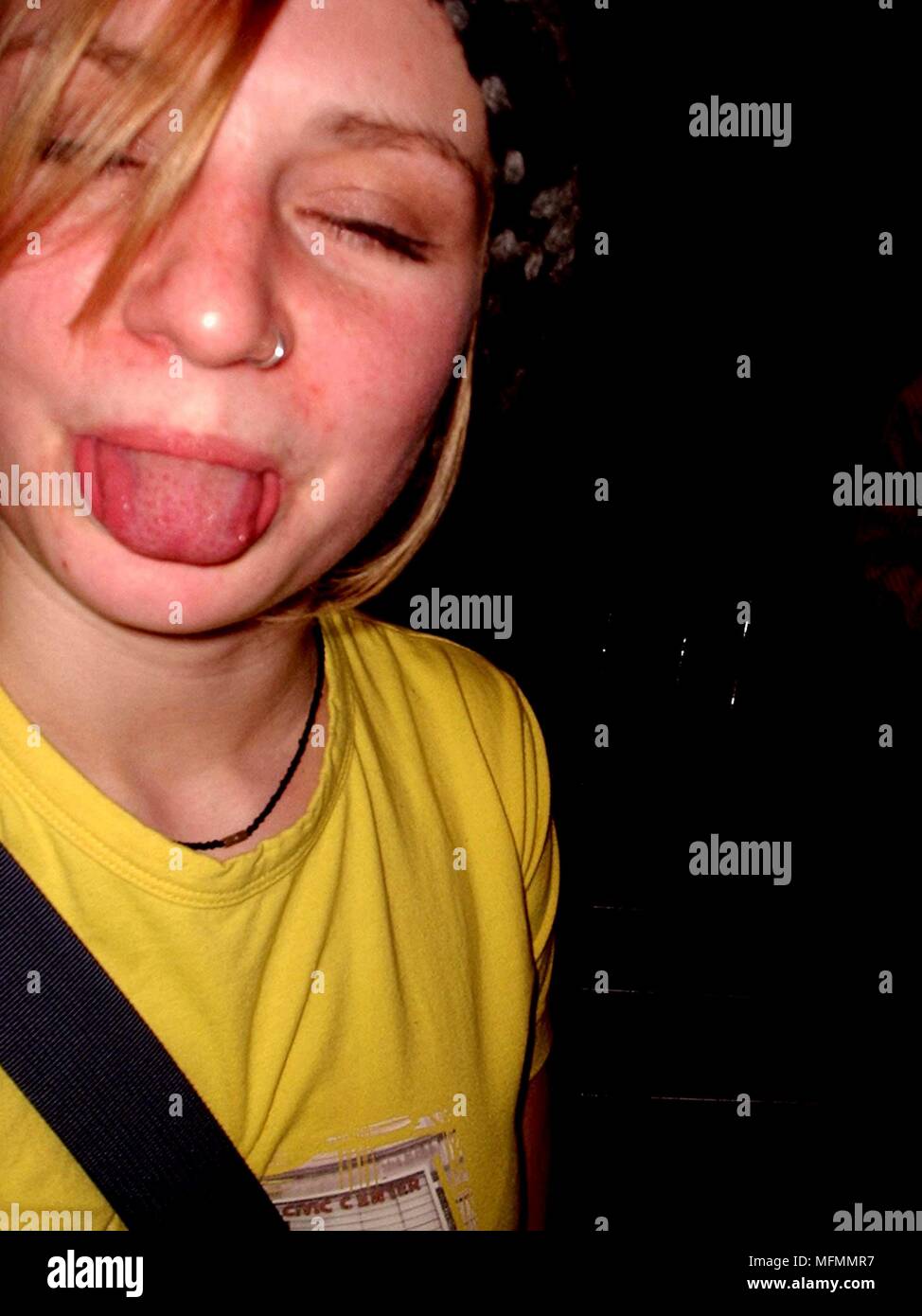 Close-up of a young woman sticking her tongue out with her eyes closed ...