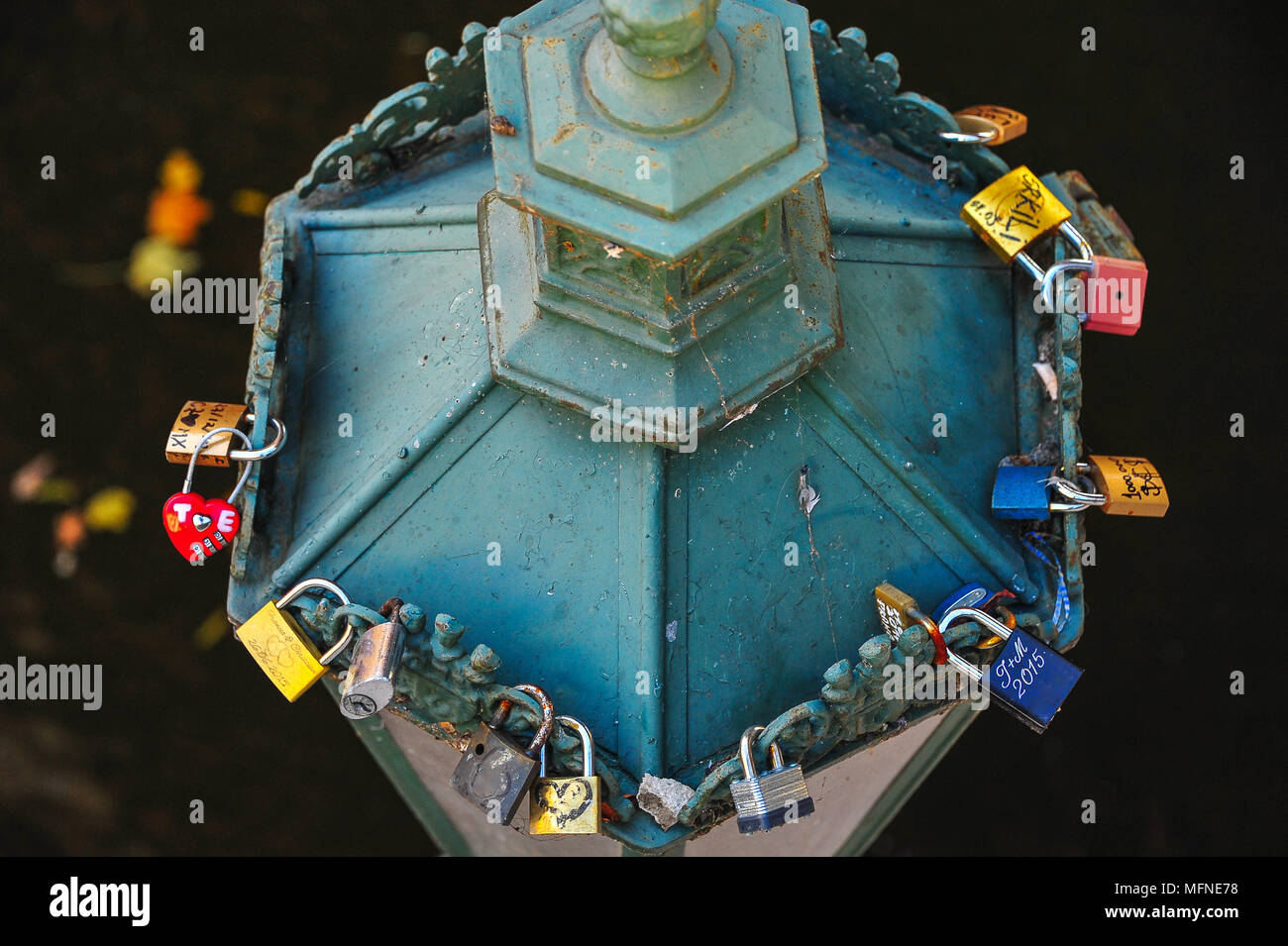 Colourful love locks decorate a bright turquoise lamp post against dark ...