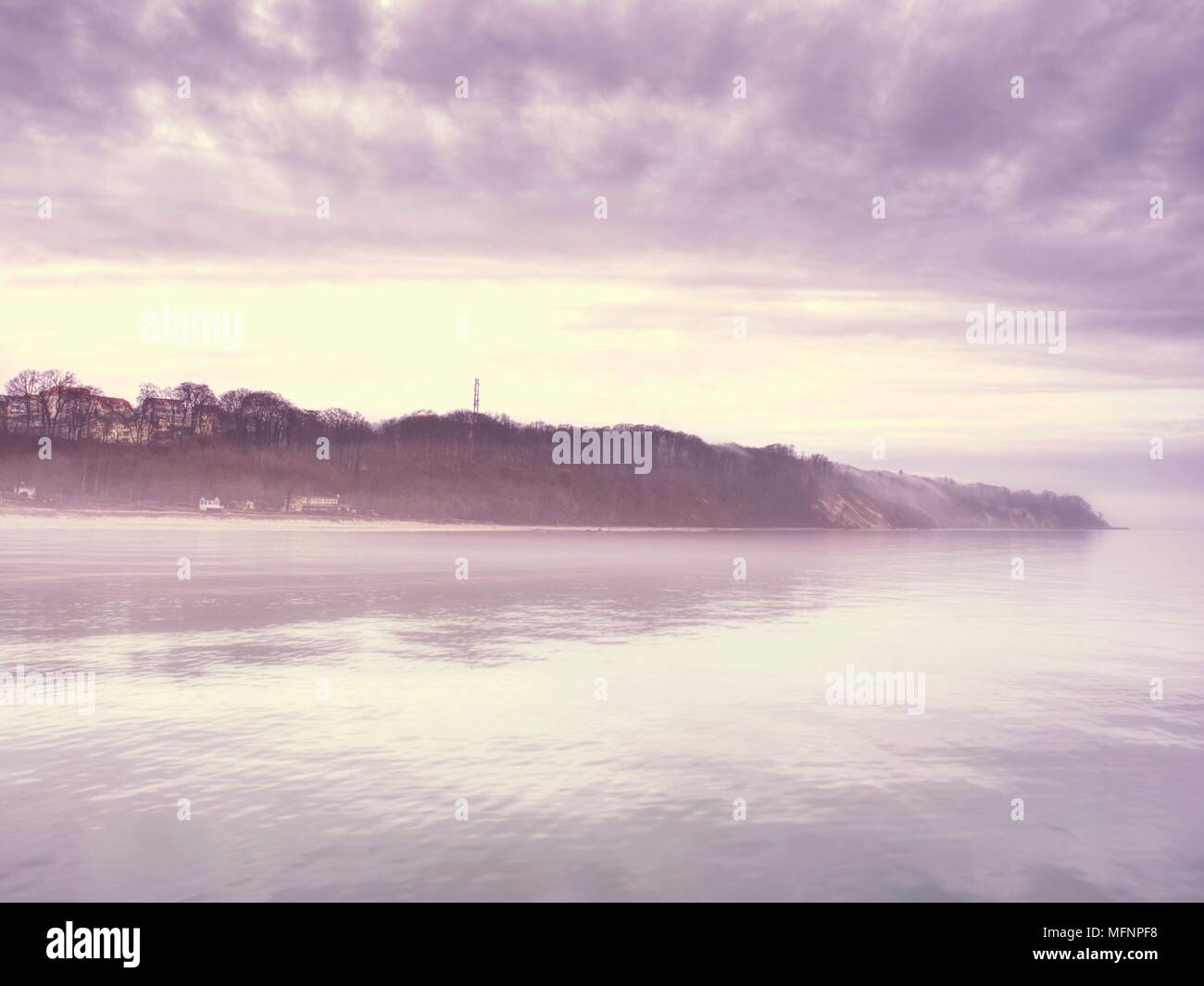 Sunset at the sea, the island is hidding in mist. Smooth water level ...