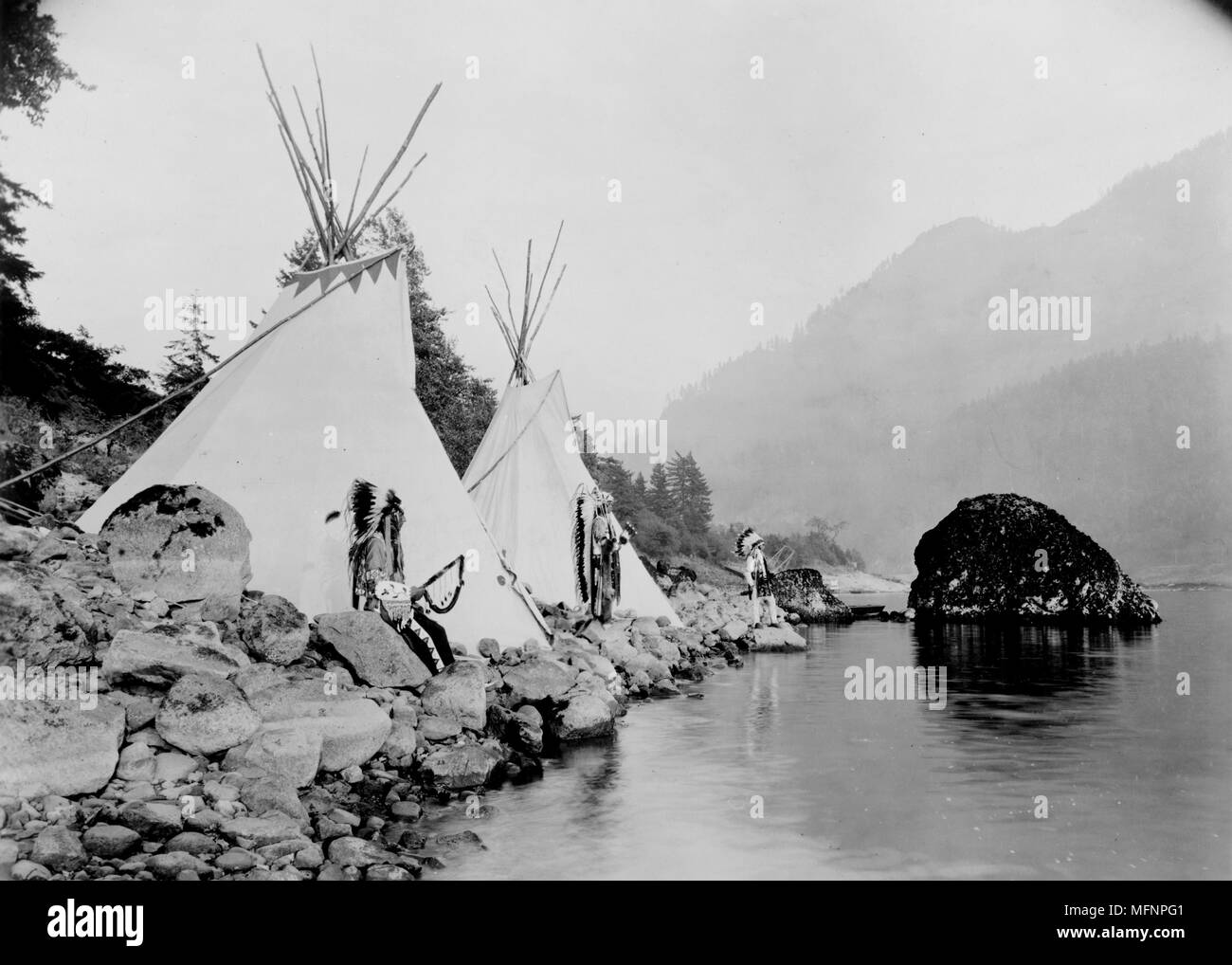 Three Native American men, probably Umatilla, stand on shore of river ...