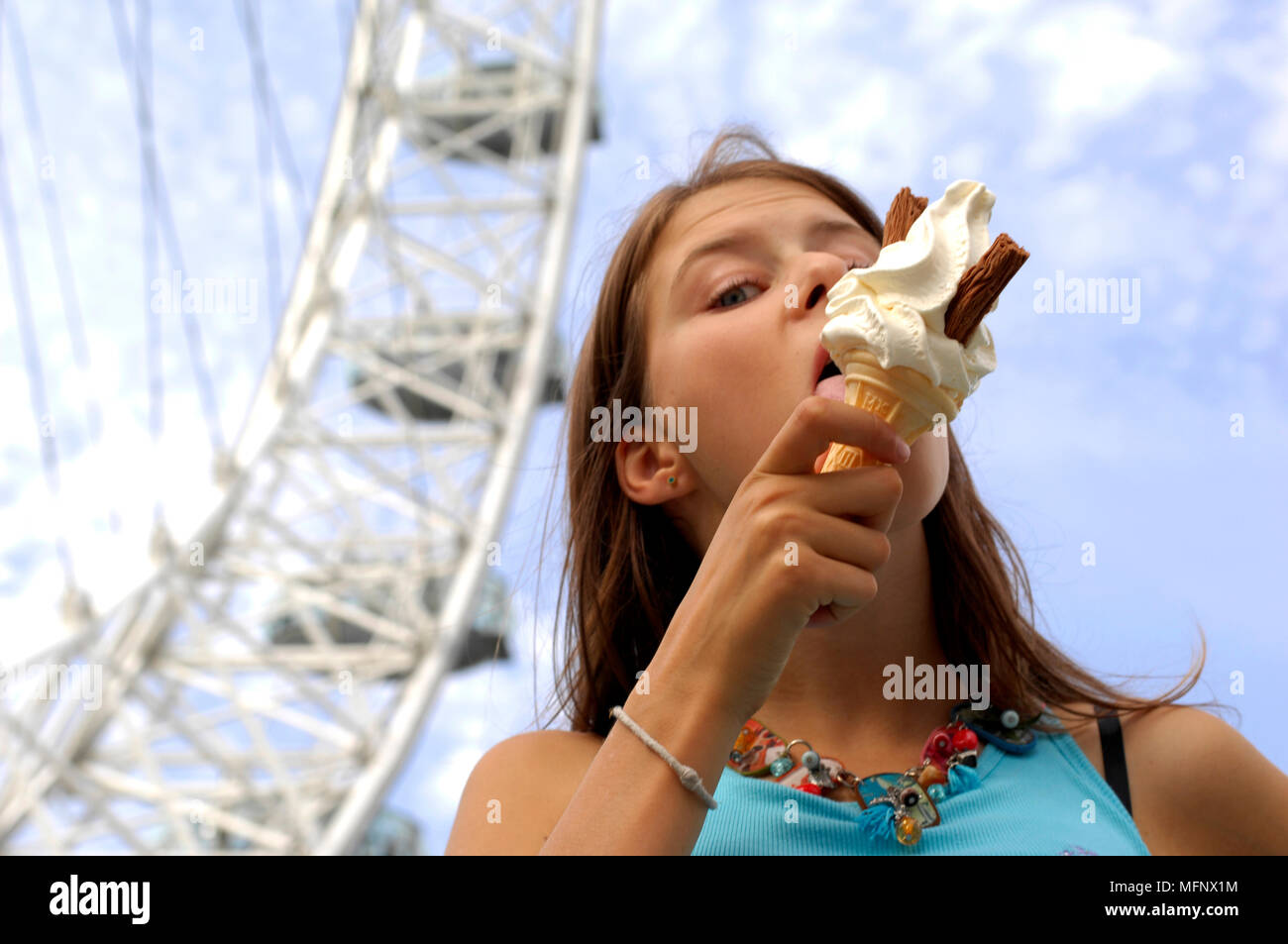 Portrait of a young woman eating an ice-cream cone with a ferris wheel ...
