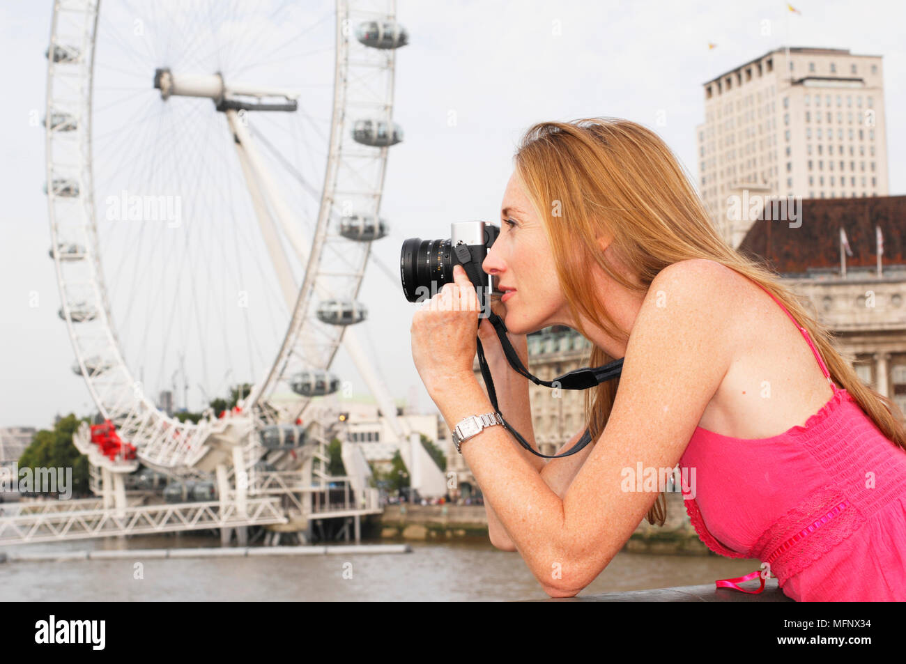 Side profile of a young woman taking a photograph in front of a ferris ...