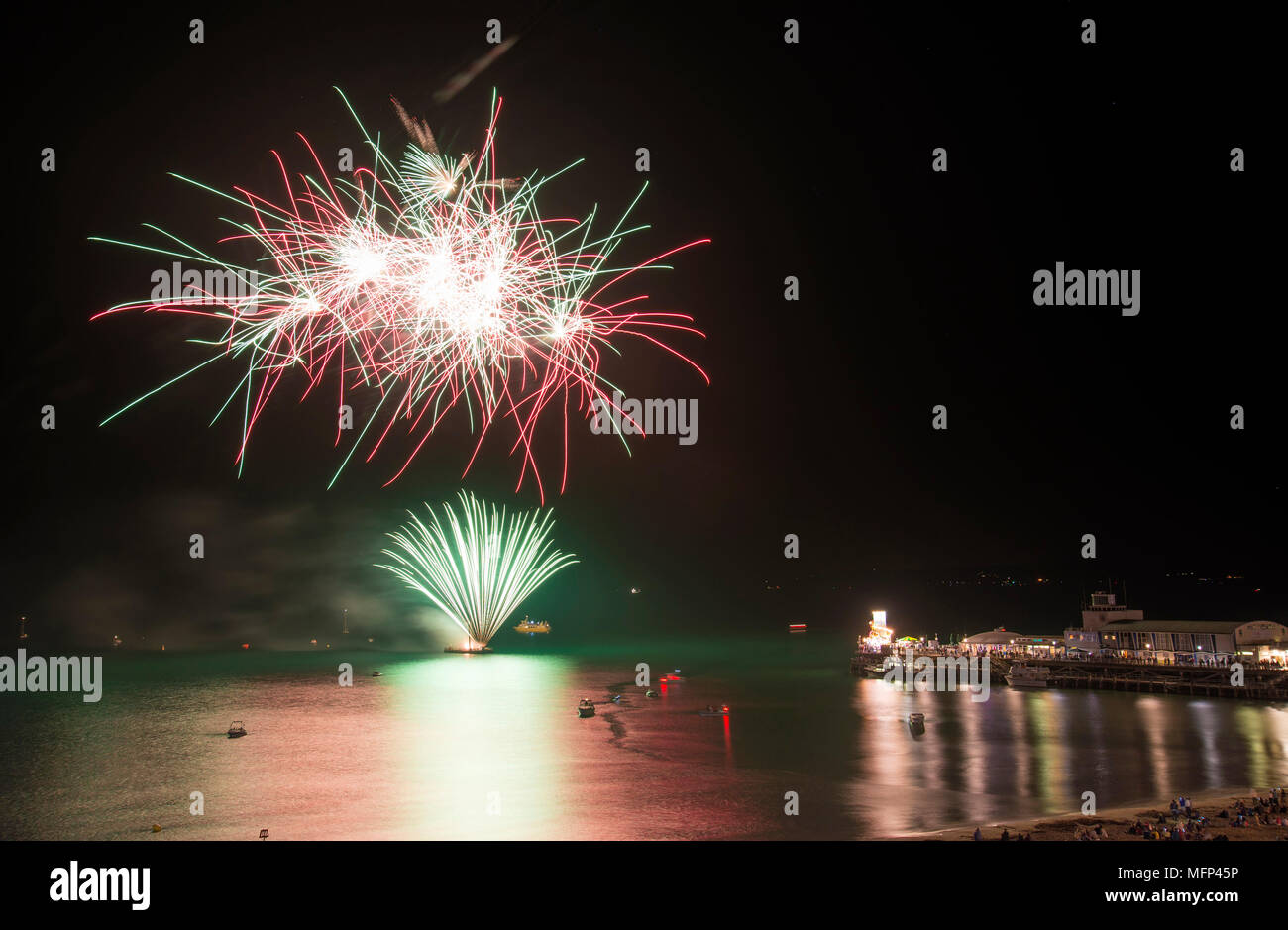 Fireworks display over sea with pier and boats in water landscape scene ...