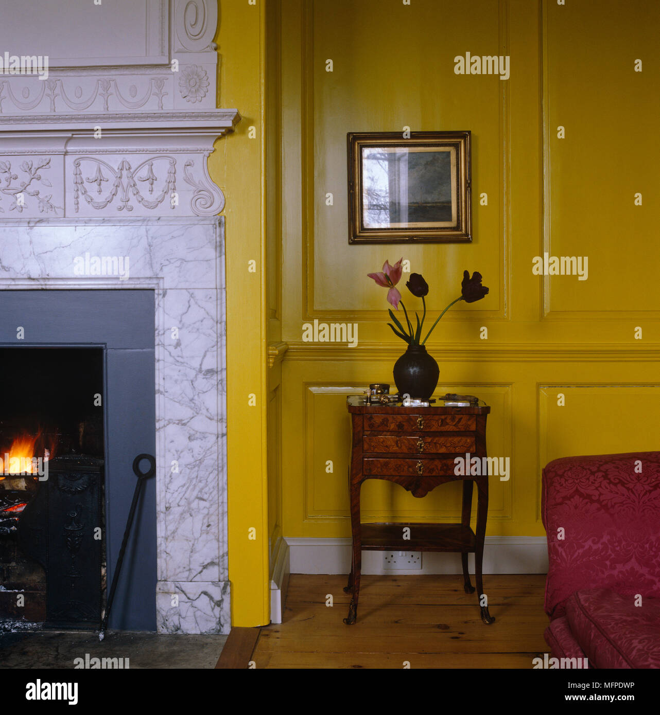 Period style table next to fireplace with lit fire and marble surround ...