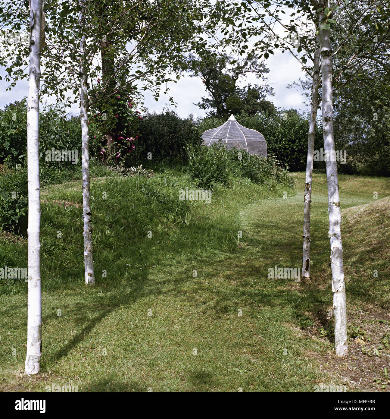 Grass pathway through trees to conical shaped structure in garden Stock ...