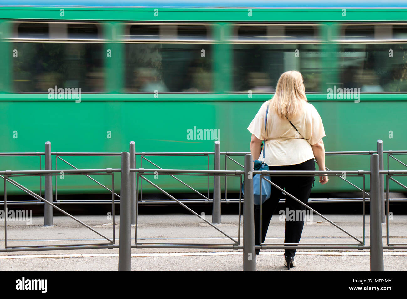 One blond plus size woman waiting at tram stop in between traffic ...
