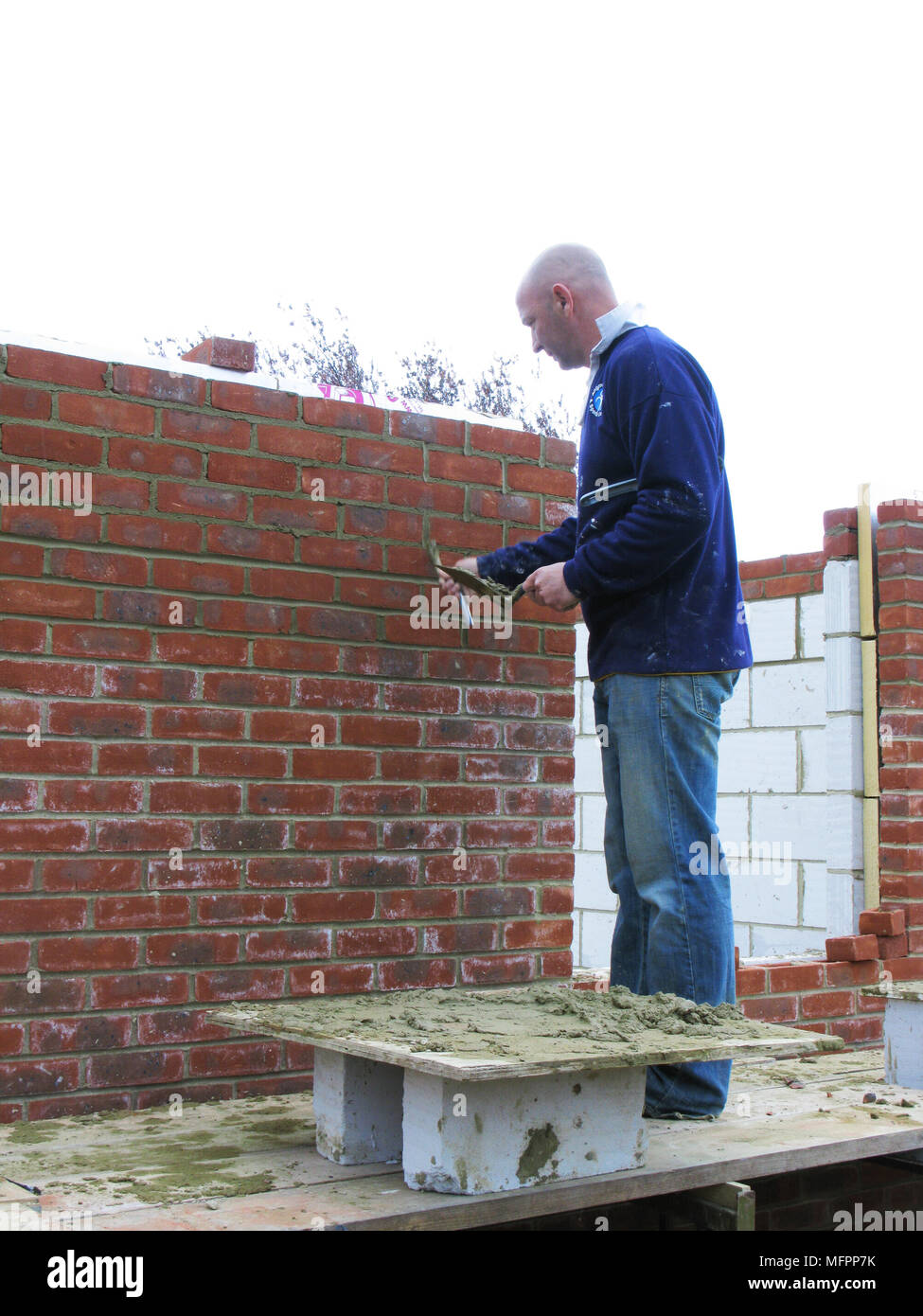 Builder / construction worker building a brick wall cementing bricks in ...