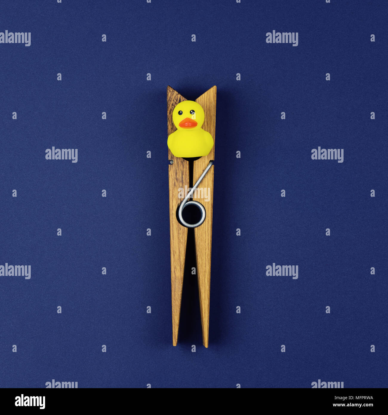 Small yellow rubber duck and large wooden clothespin on blue background ...