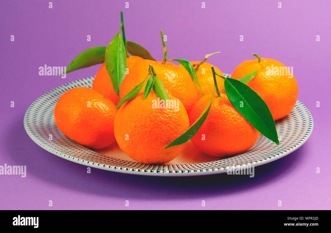 Bright plate of clementines against a mauve background make an ...