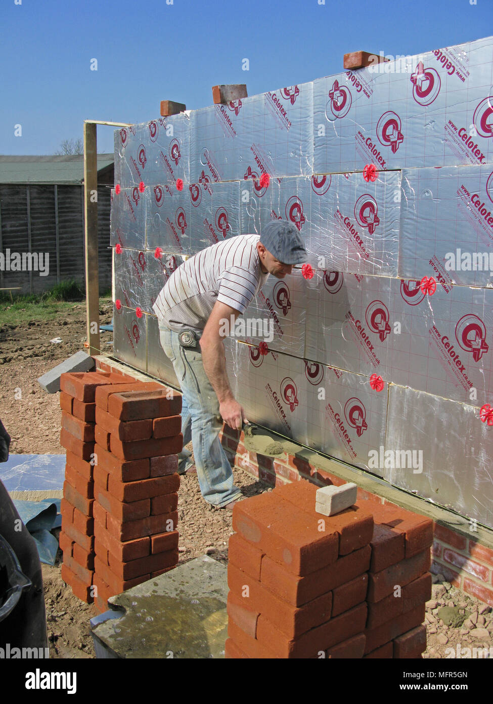 Builder / construction worker building a brick wall cementing bricks in ...