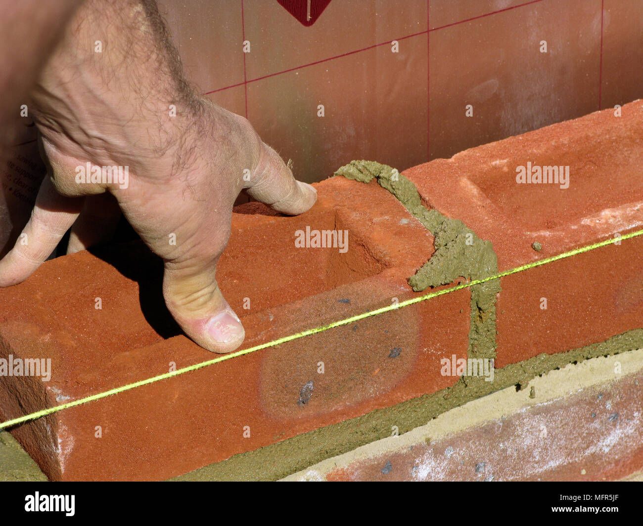 Builder / construction worker building a brick wall cementing bricks in ...