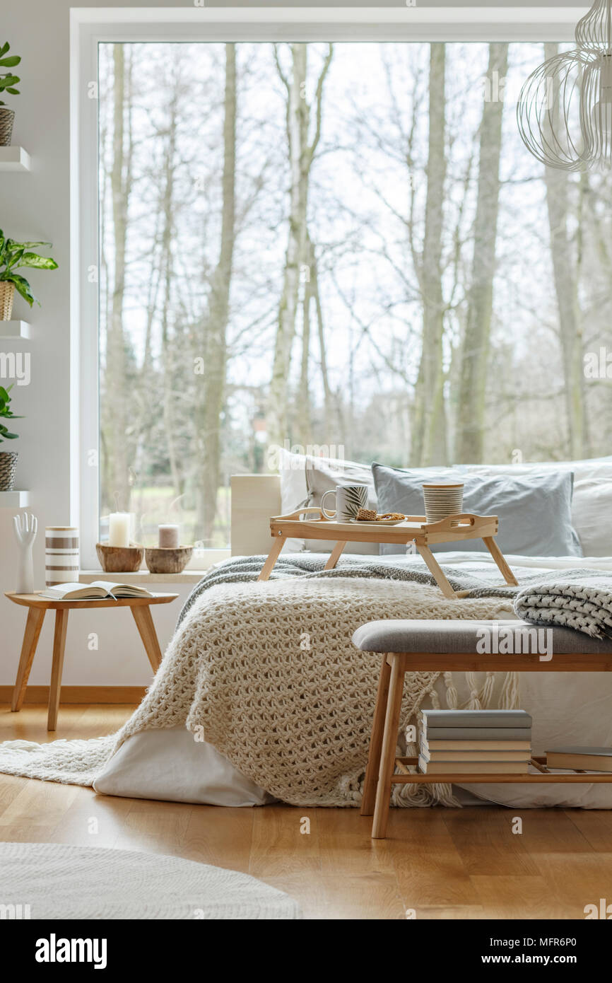Knit blanket on bed next to wooden table against the window in natural ...