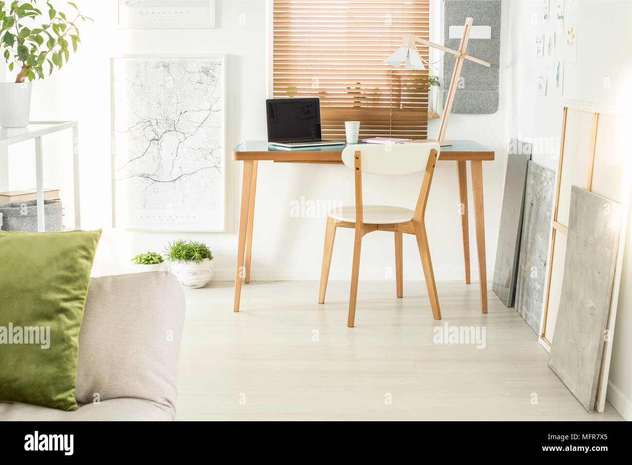 Wooden desk with a laptop, poster, paintings and chair in a simple home ...