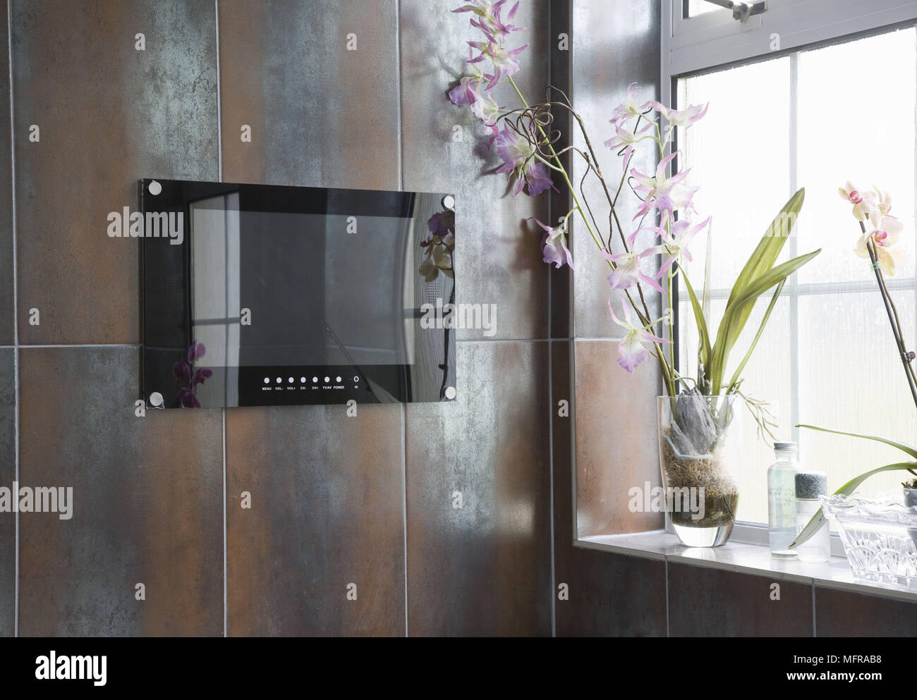 Wall mounted television screen next to flower arrangements on window ...