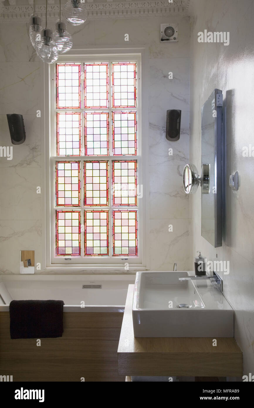 Washbasin on unit next to bathtub beneath window with red stained glass ...
