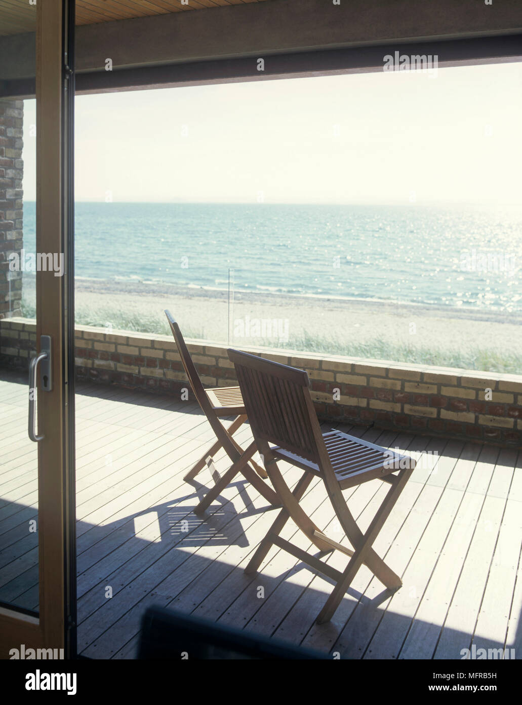 Two wooden chairs on decking facing beach Stock Photo - Alamy